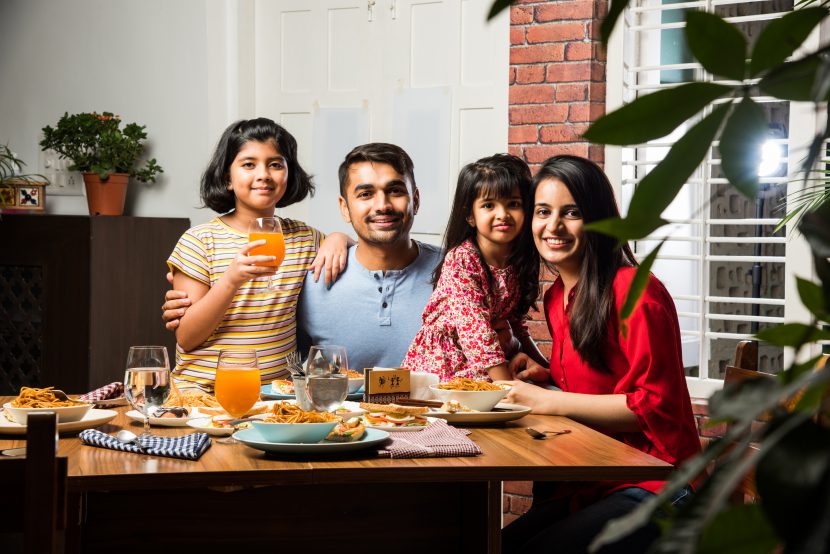 Indian,Young,Family,Of,Four,Eating,Food,At,Dining,Table - Humanium