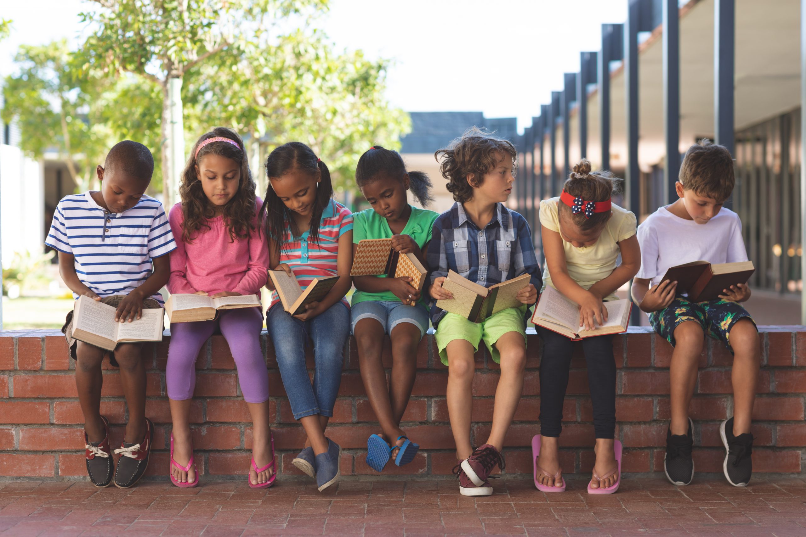 Front,View,Of,Diverse,Students,Reading,Book,While,Sitting,On - Humanium