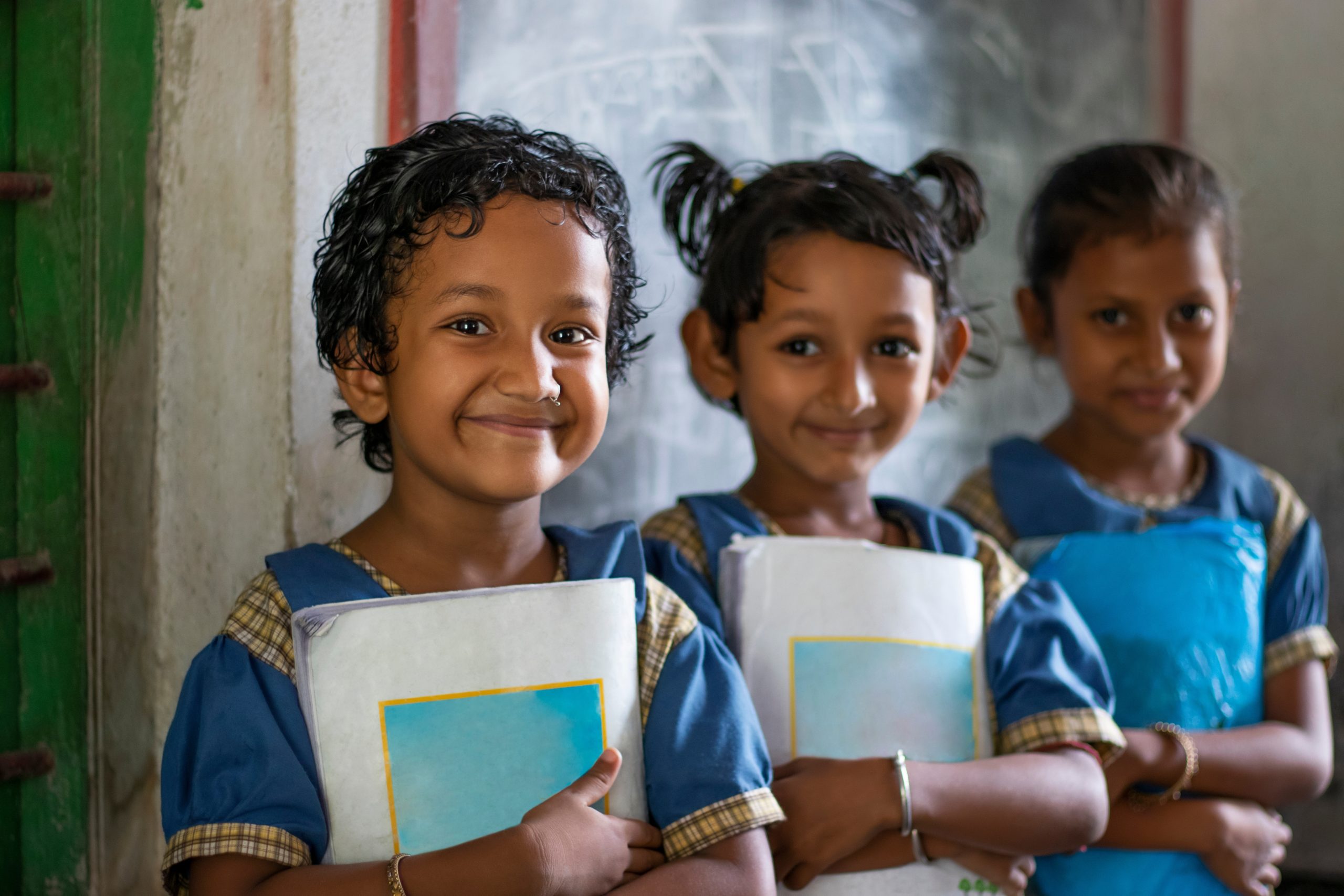 Three,School,Children's,Holding,Books,Standing,At,School - Humanium